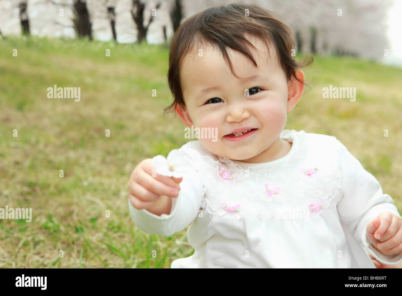 Japan, Saitama Prefecture, Baby girl sitting on grass and smiling ...