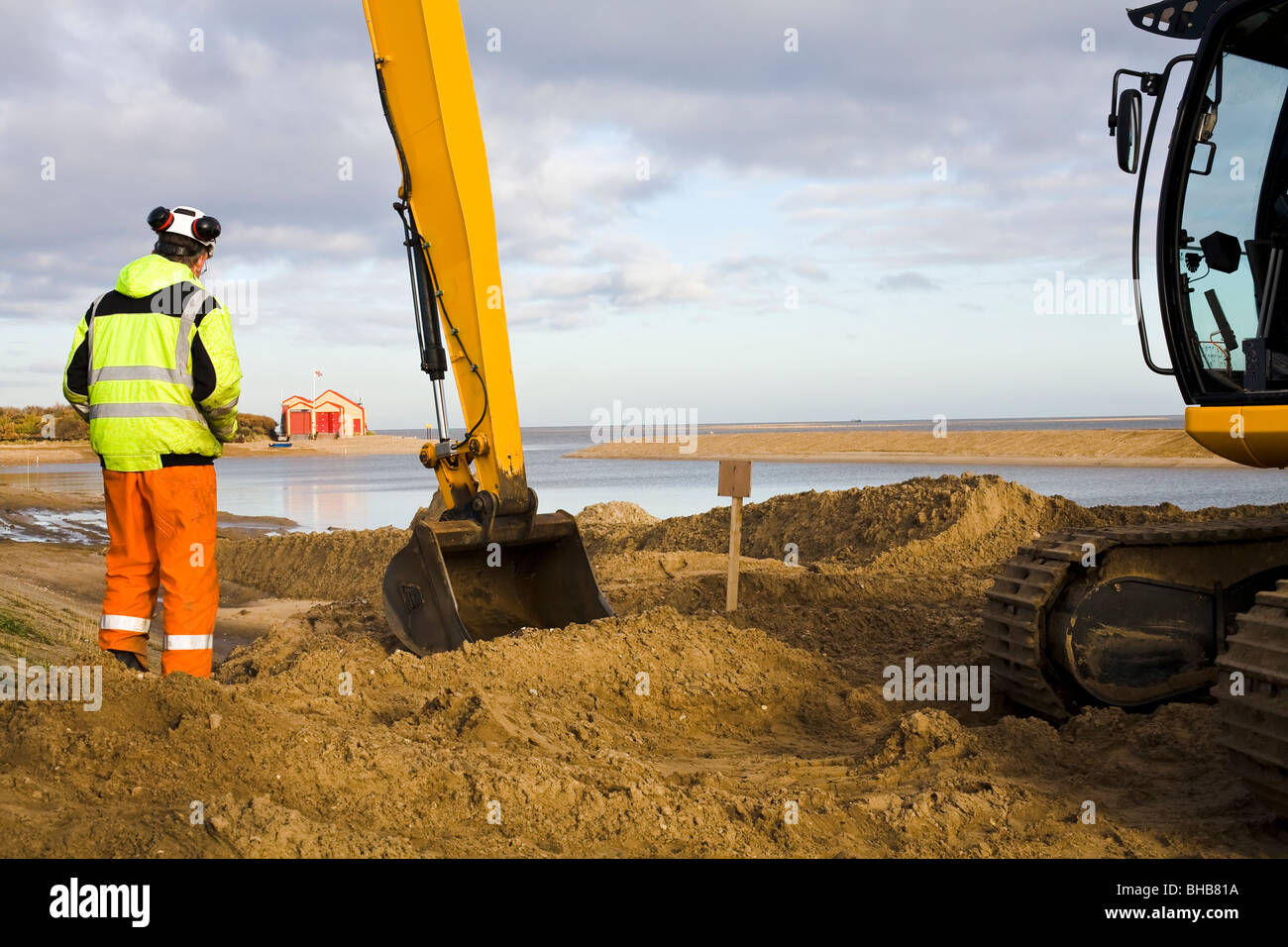 engineer supervising a digger that is excavating a new harbour for ...