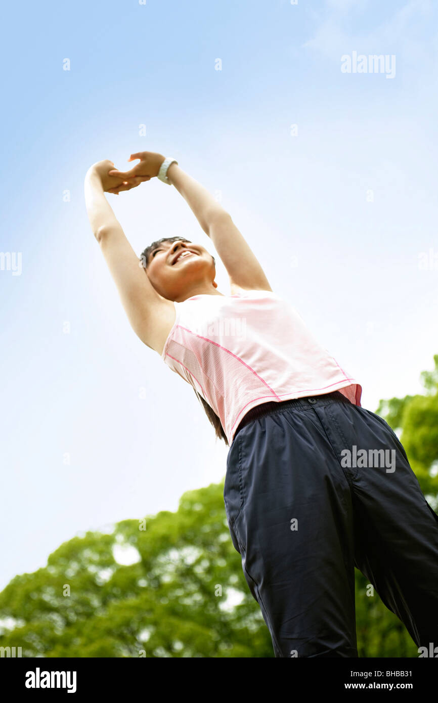 Japan, Osaka Prefecture, Woman stretching arms, smiling, low angle view ...