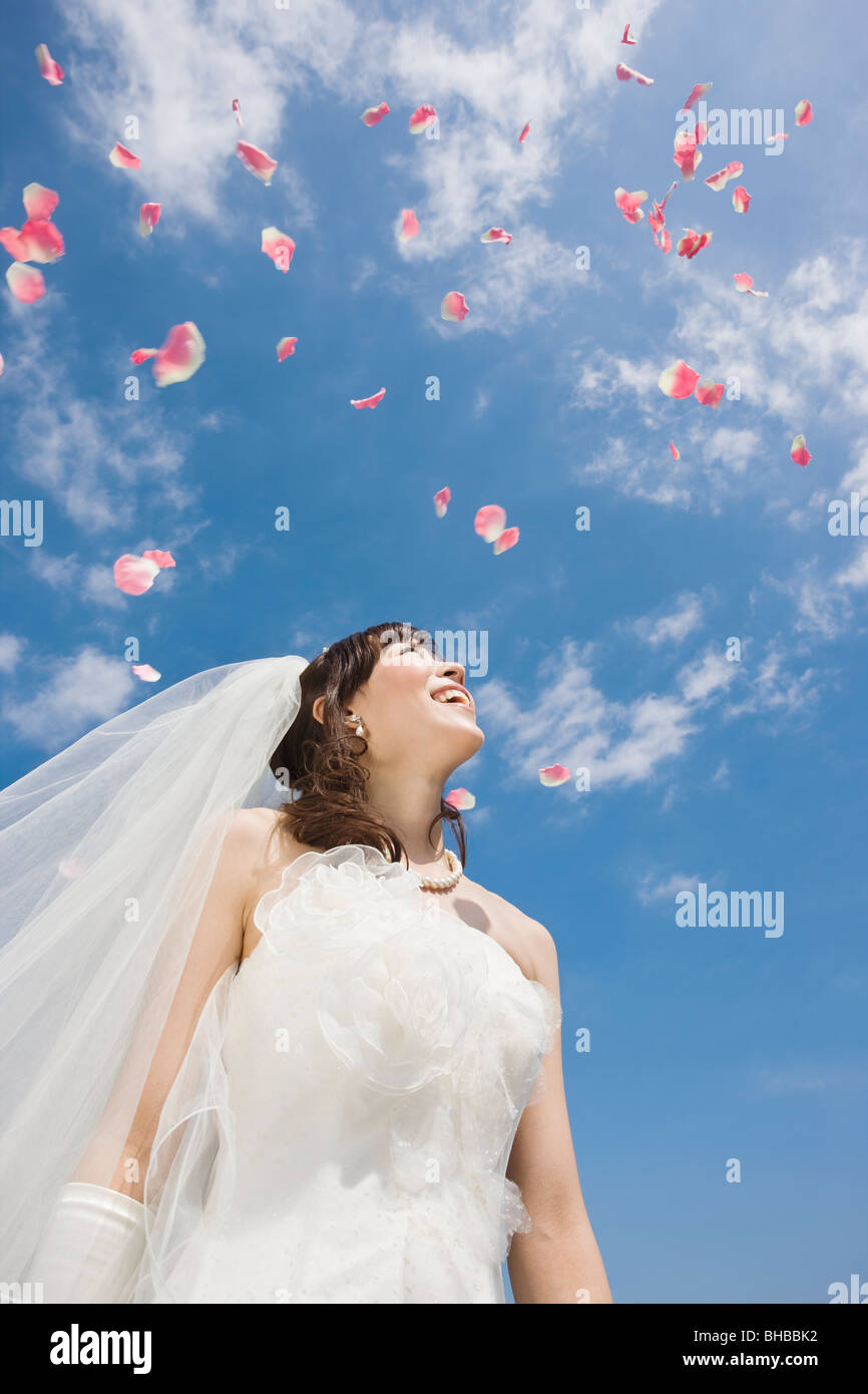 a cheerful bride with rose petals falling down on her, low angle view ...