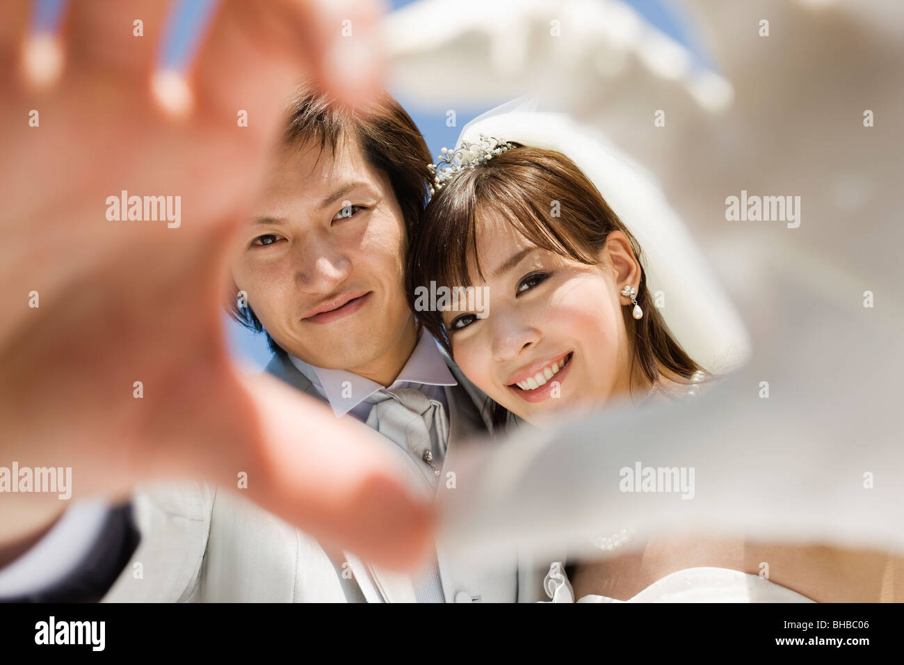 portrait of a smiling bride and groom making a heart symbol with their ...