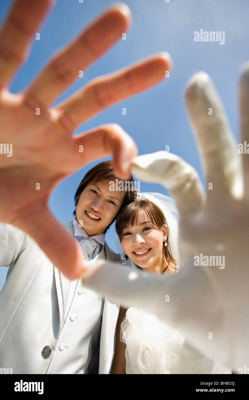 portrait of a smiling bride and groom making a heart symbol with their ...