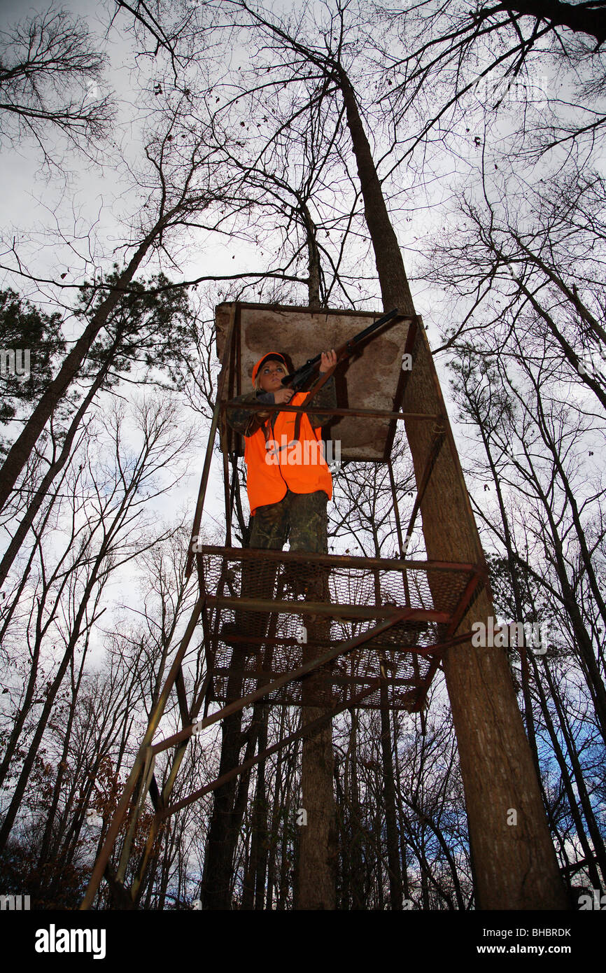 YOUNG WOMAN 21 Y.O. FEMALE HUNTER IN A TREE STAND HOLDING RIFLE ORANGE ...