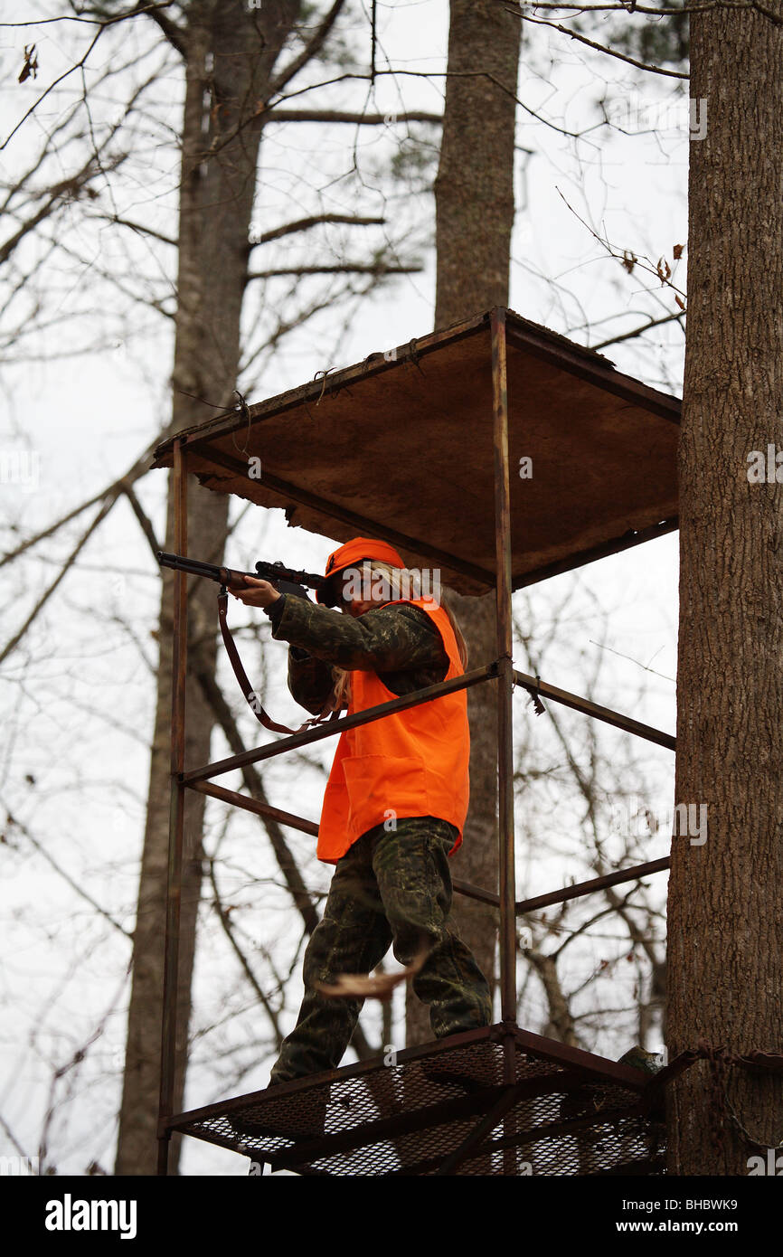 YOUNG WOMAN 21 Y.O. FEMALE HUNTER IN A TREE STAND HOLDING RIFLE ORANGE ...