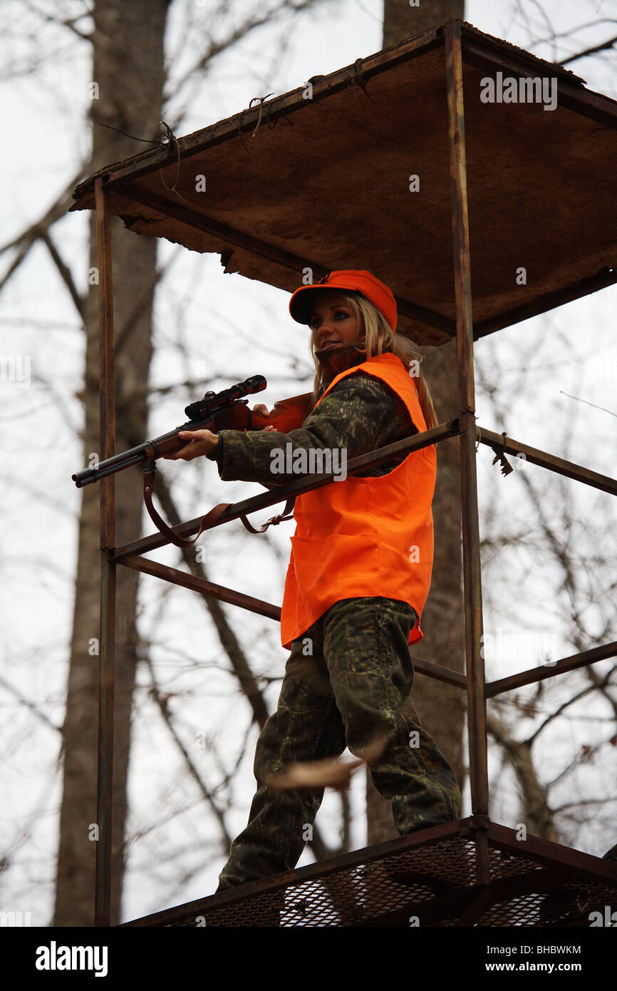 YOUNG WOMAN 21 Y.O. FEMALE HUNTER IN A TREE STAND HOLDING RIFLE ORANGE ...