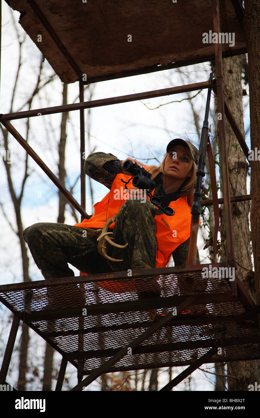 YOUNG WOMAN 21 Y.O. FEMALE HUNTER IN A TREE STAND HOLDING RIFLE ORANGE ...