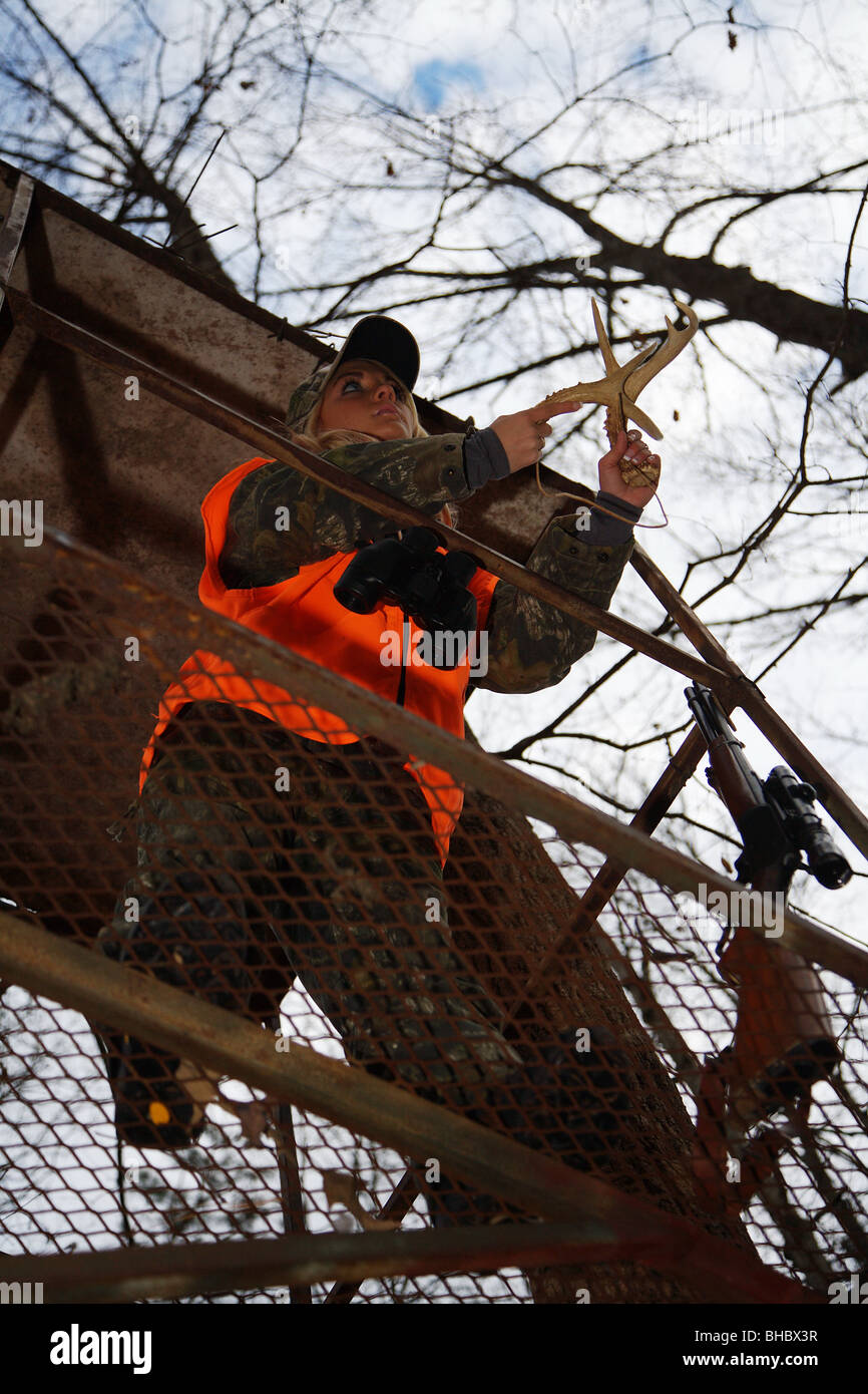 YOUNG WOMAN 21 Y.O. FEMALE HUNTER IN A TREE STAND HOLDING RIFLE ORANGE ...