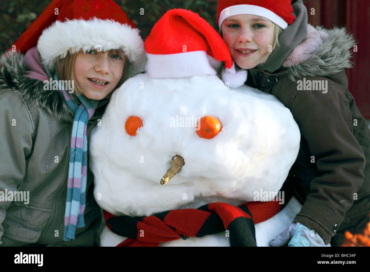 Two girls trying to look like a snowman which has a hat and scarf ...