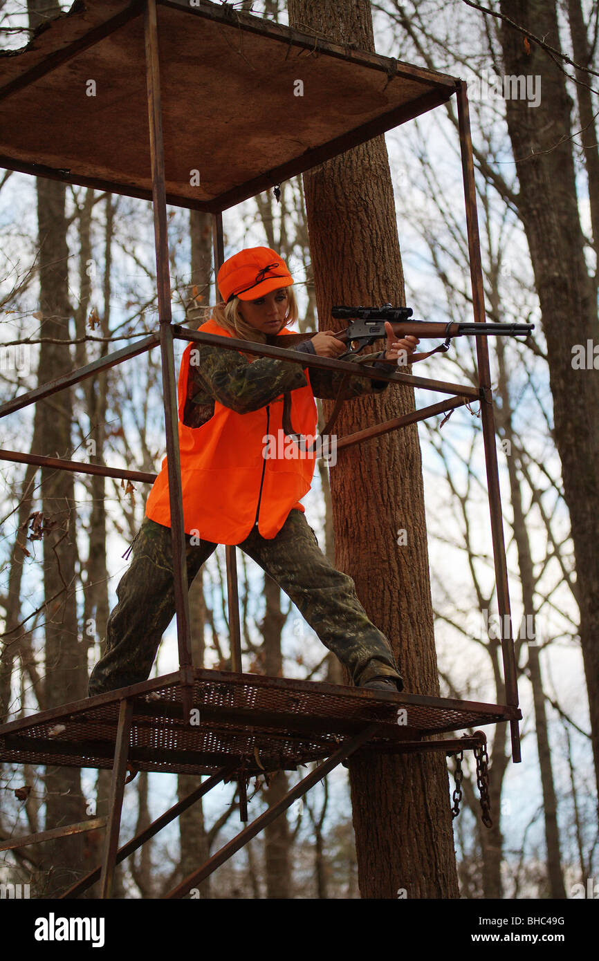 YOUNG WOMAN 21 Y.O. FEMALE HUNTER IN A TREE STAND HOLDING RIFLE ORANGE ...