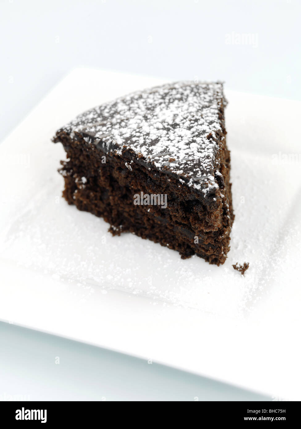 A piece of chocolate mud cake isolated against a pale blue background ...