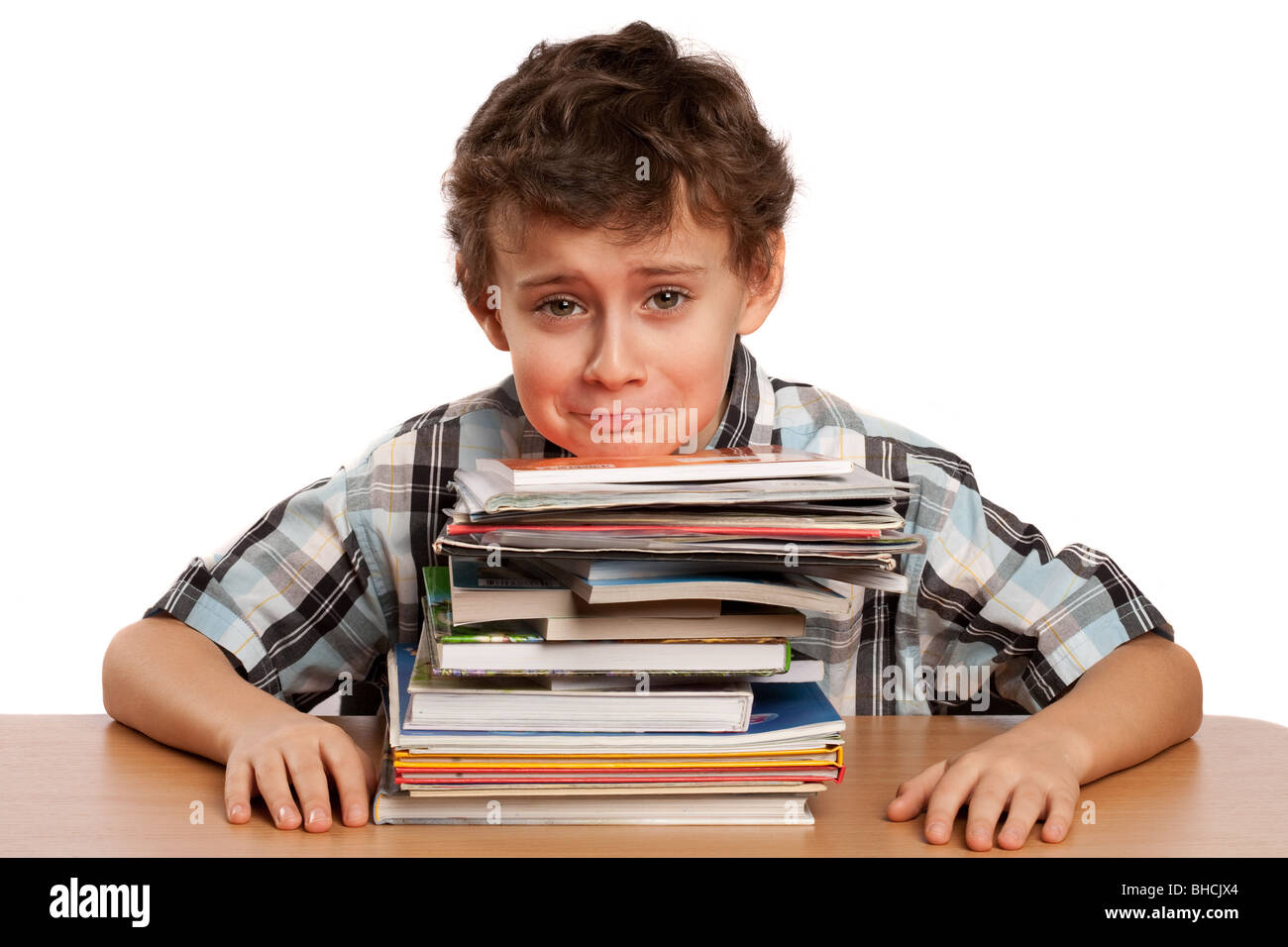 Portrait of a schoolboy overwhelmed by the stack of books on his desk ...
