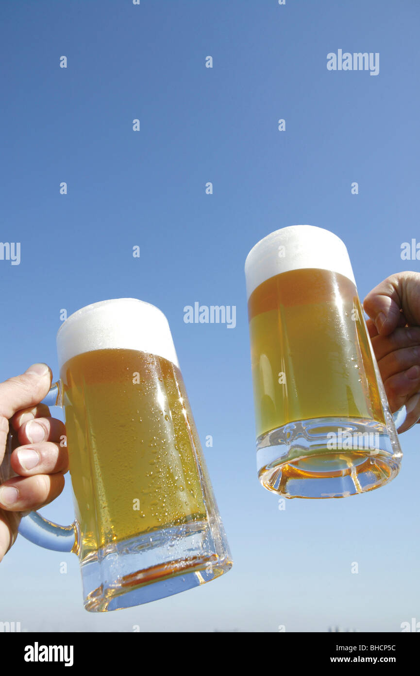 Hands toasting with glass of beer against blue sky blue background ...
