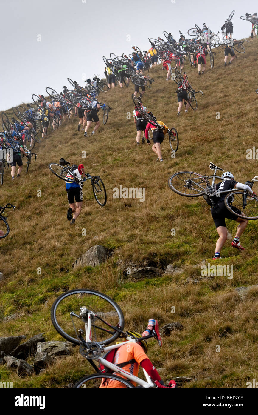 Crowd of cyclists carry their bicycles up a mountain during the Three ...