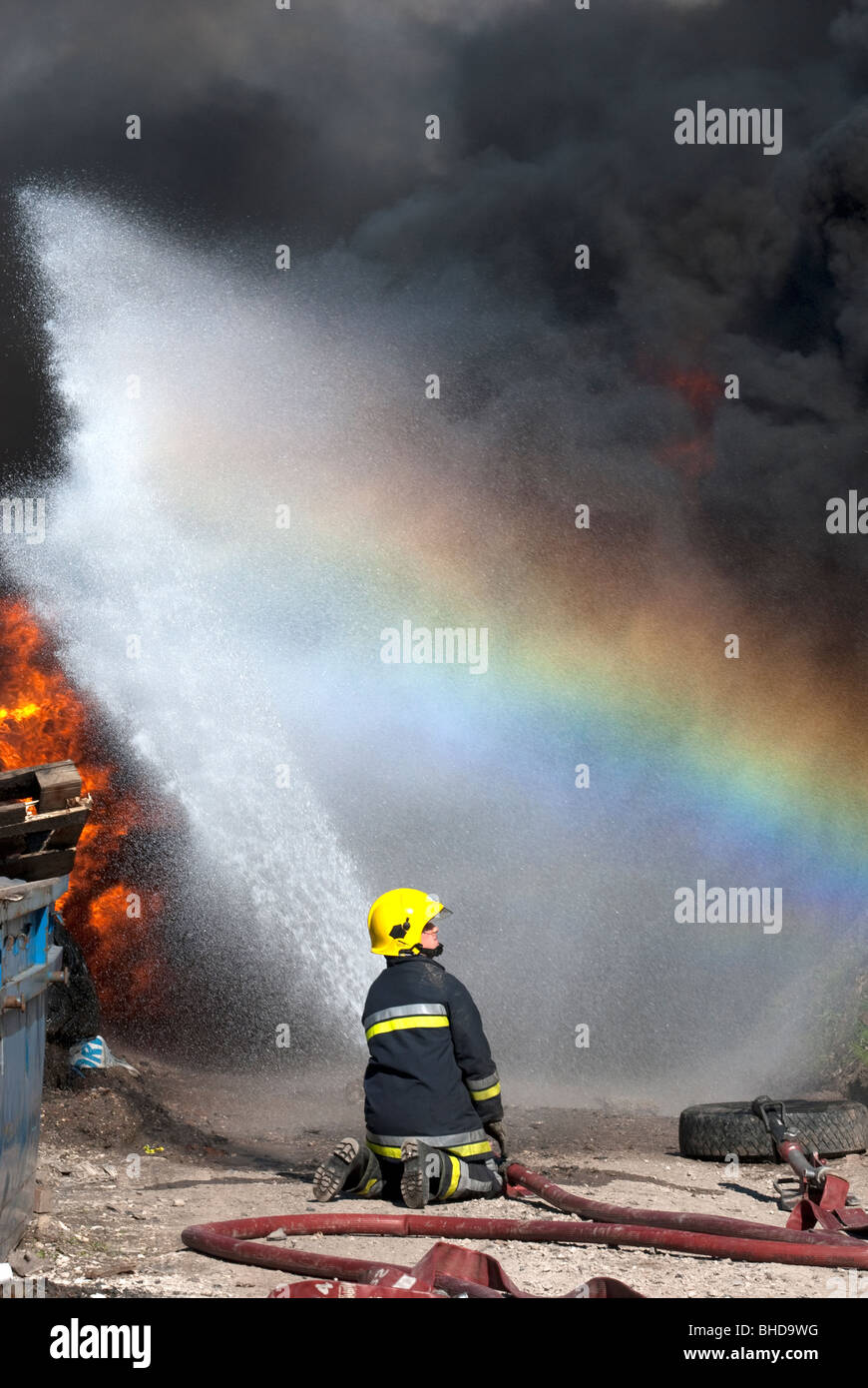 Fireman with ground monitor spraying water in sunlight giving rainbow ...