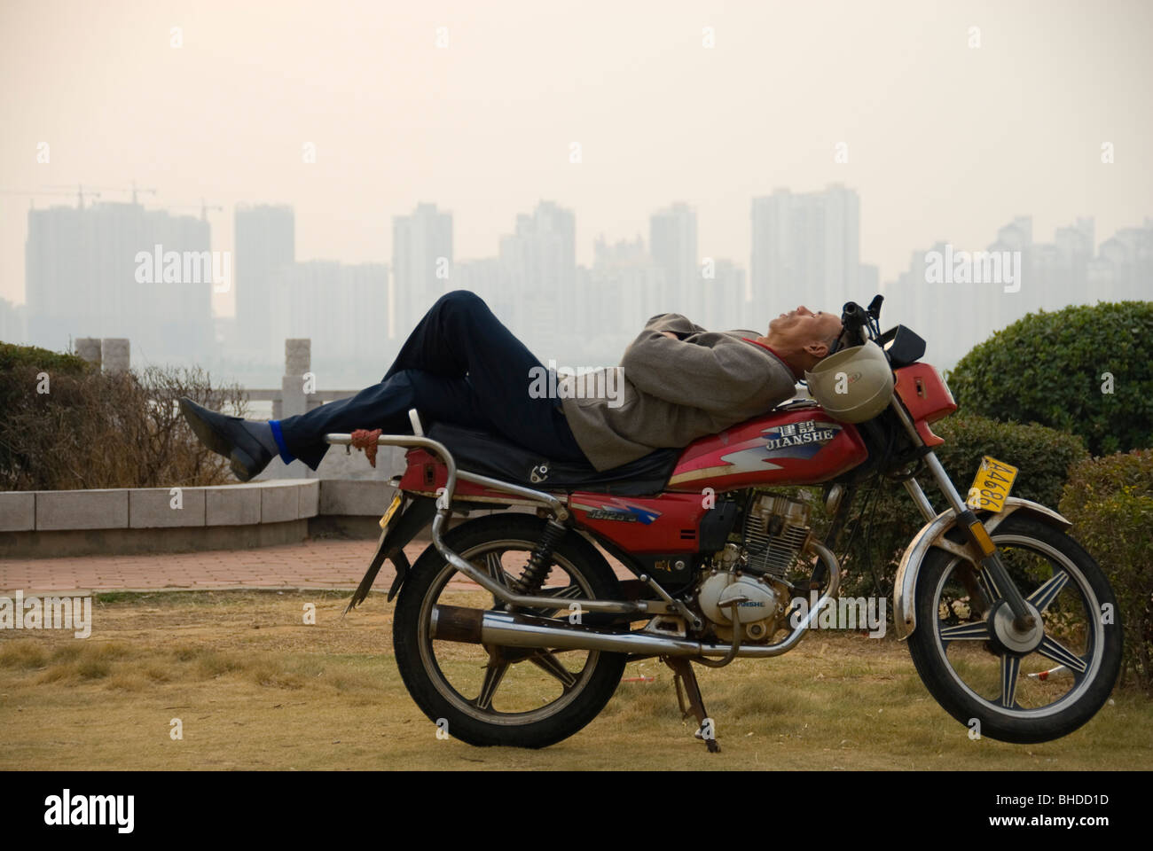 Tired motor cyclist taking a rest on his motorcycle in a park. Jiangxi ...