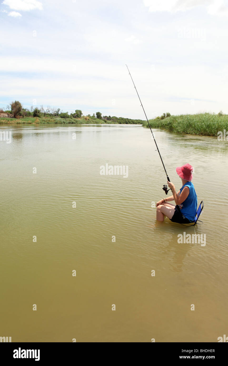 A woman sits fishing in the wtaer of the Orange River near Upington ...
