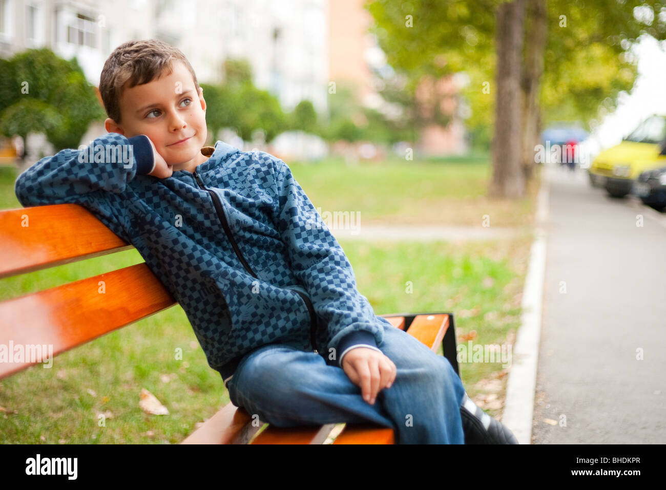 Cute kid sitting on a bench in a park Stock Photo - Alamy