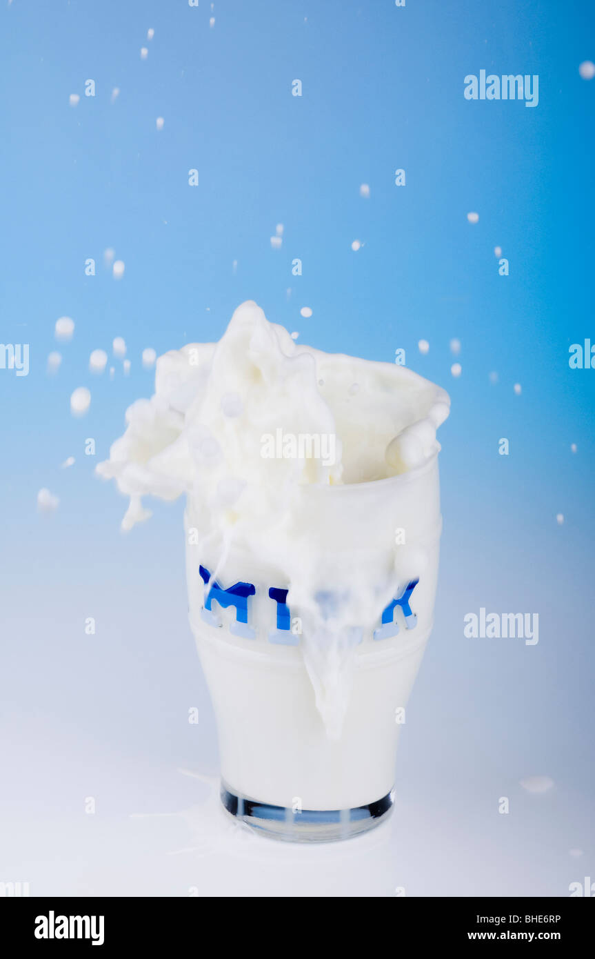 Milk being splashed out from a glass on blue Stock Photo - Alamy