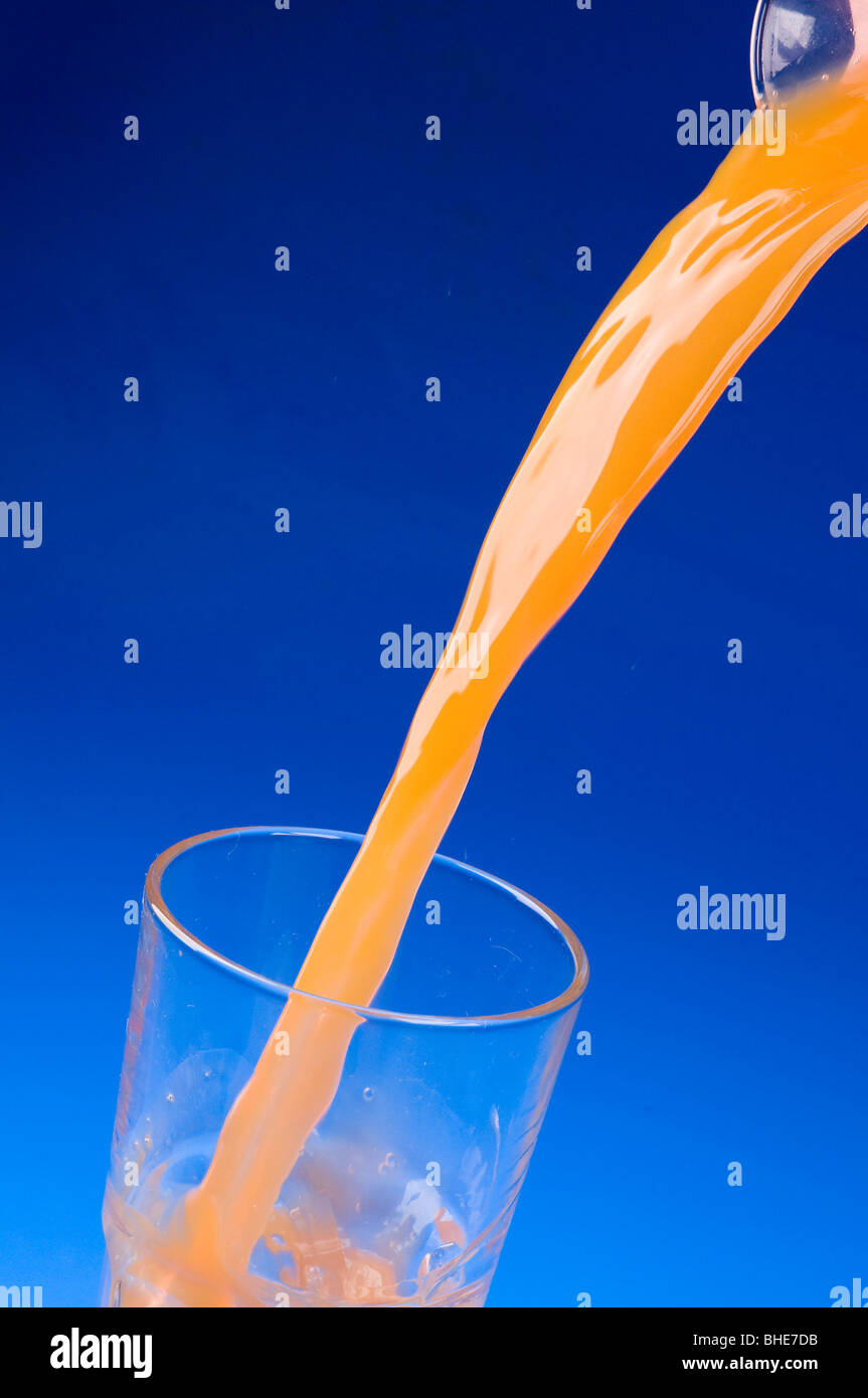 Stream of fresh orange juice over blue background Stock Photo - Alamy