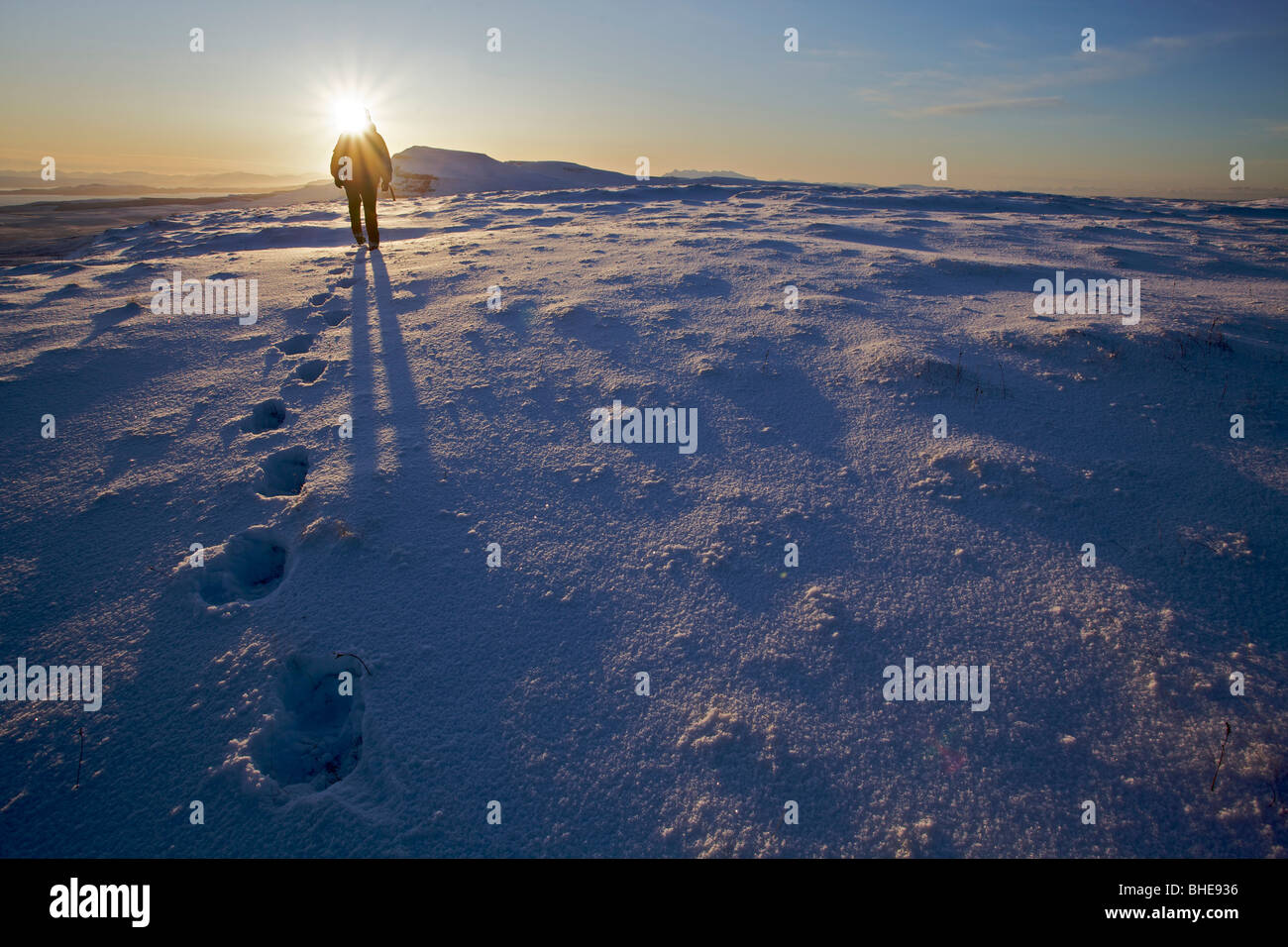 Hiker walking through the snow into the sun, Isle of Skye, Scotland ...