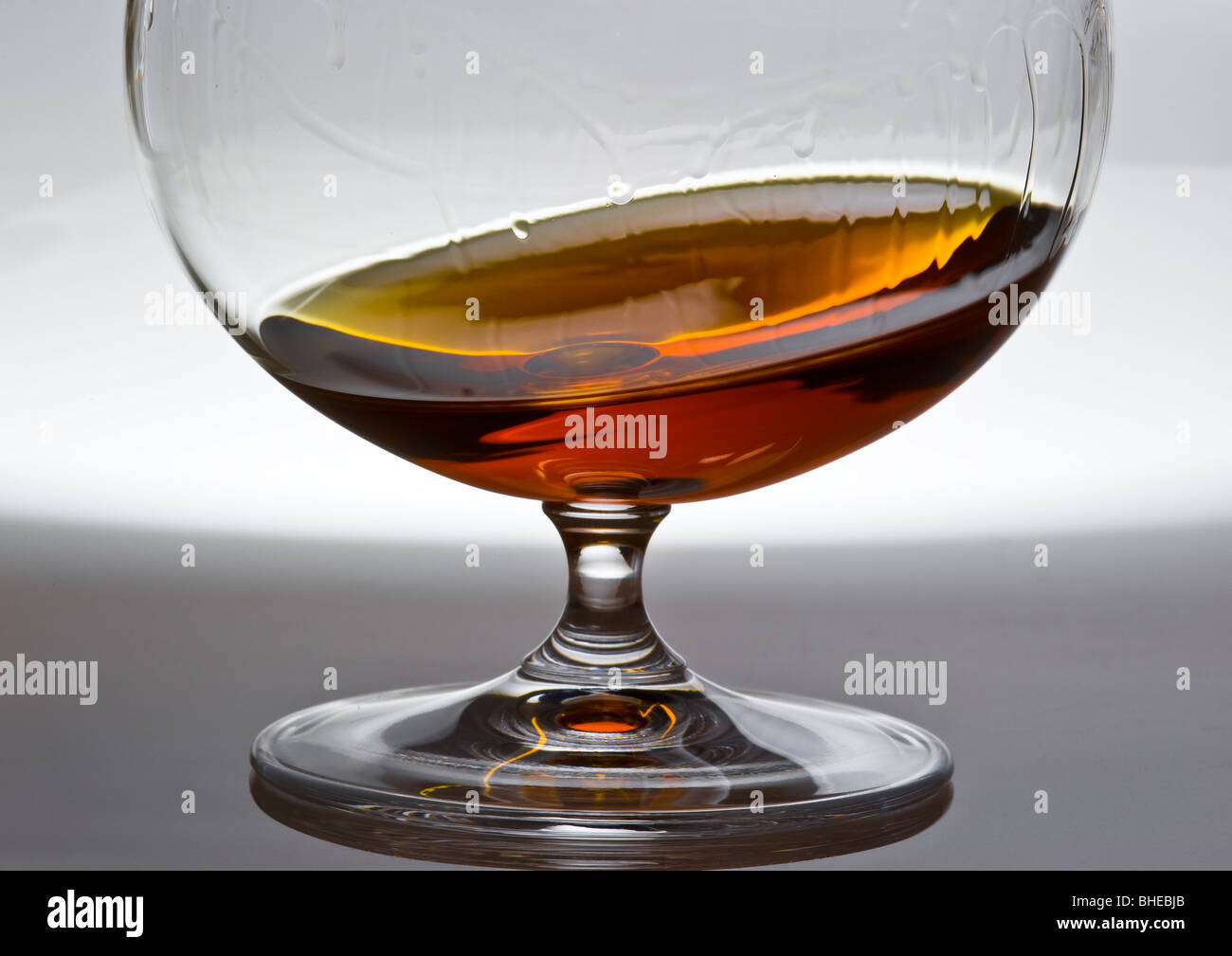 Shaking liquid of alcohol of orange colour in a glass on a grey ...