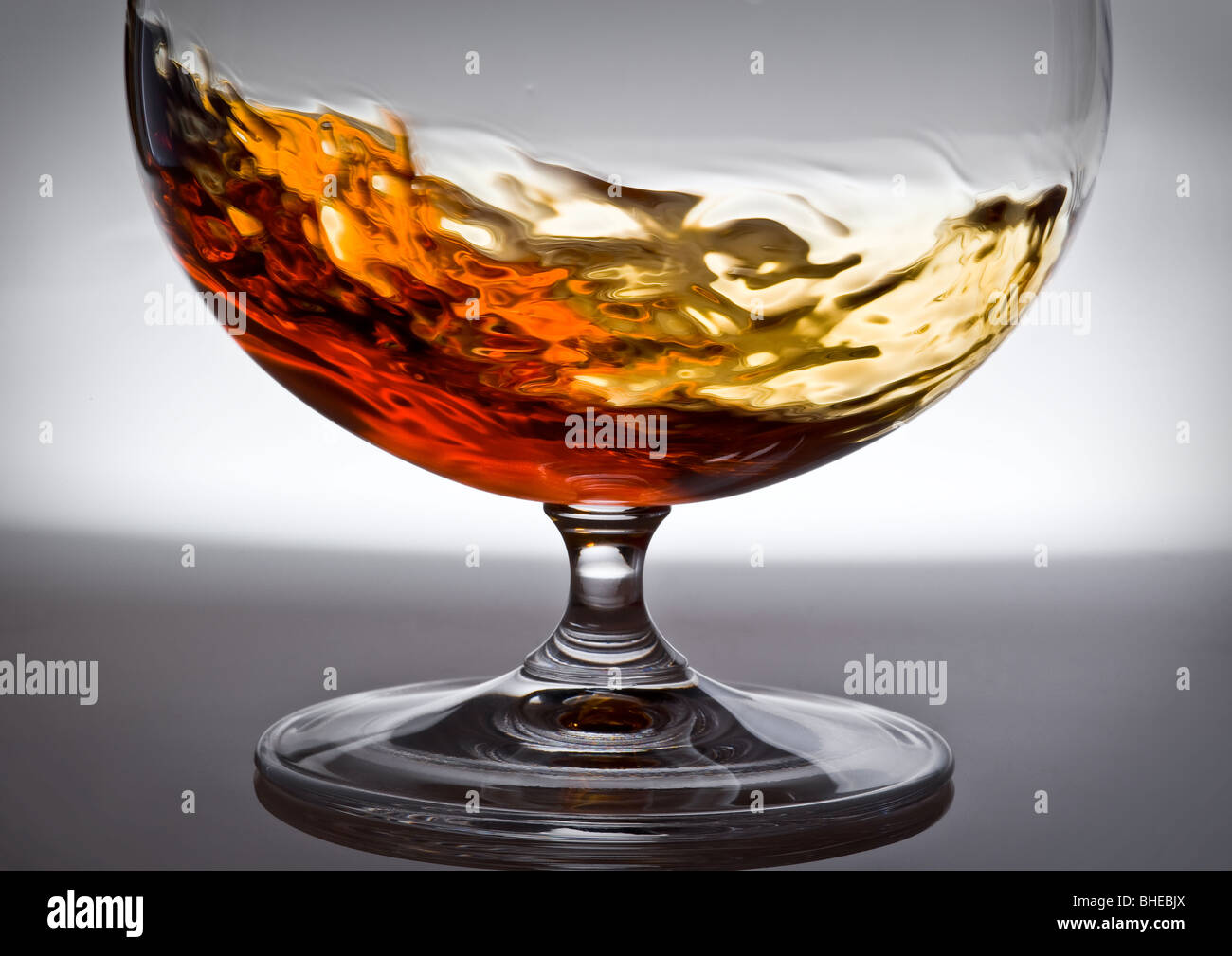 Raging liquid of alcohol of orange colour in a glass on a grey ...