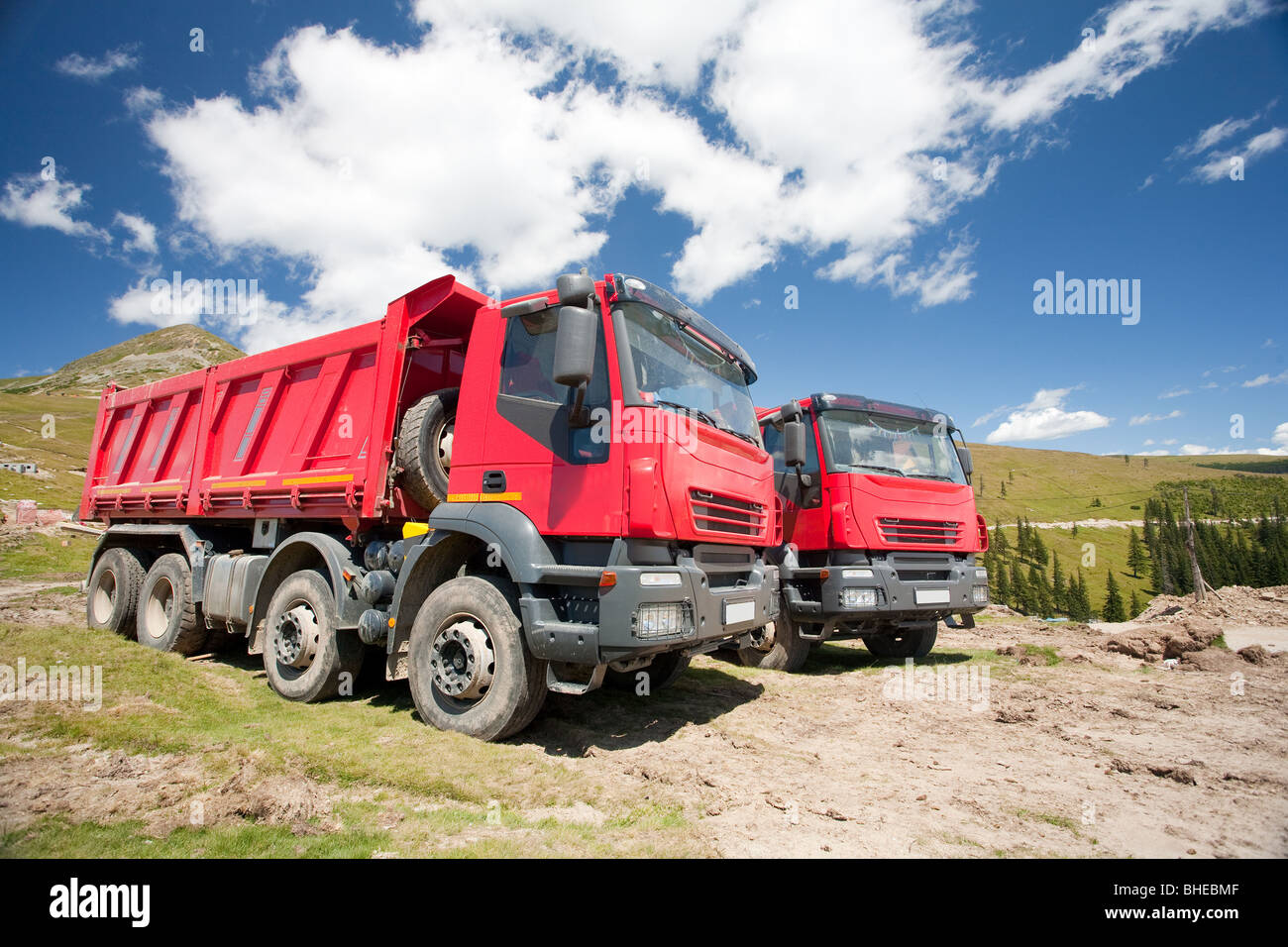 Two large red dump trucks at construction site, in a sunny summer day ...