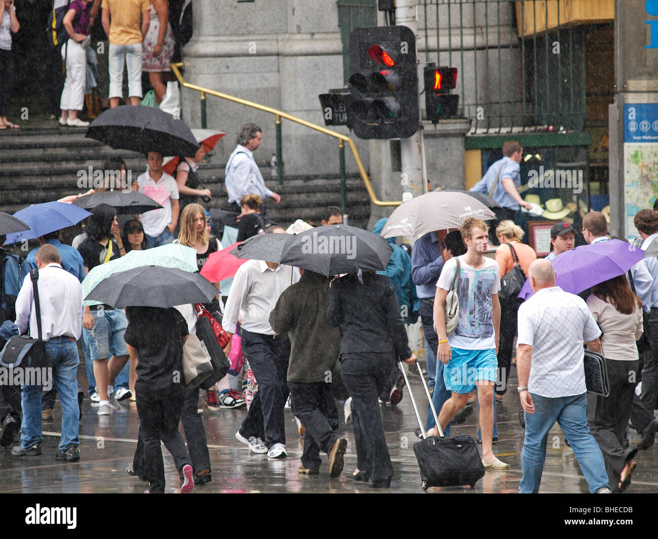 COMMUTERS HOLDING UMBRELLAS WHILST CROSSING ROAD AT FLINDERS STREET ...