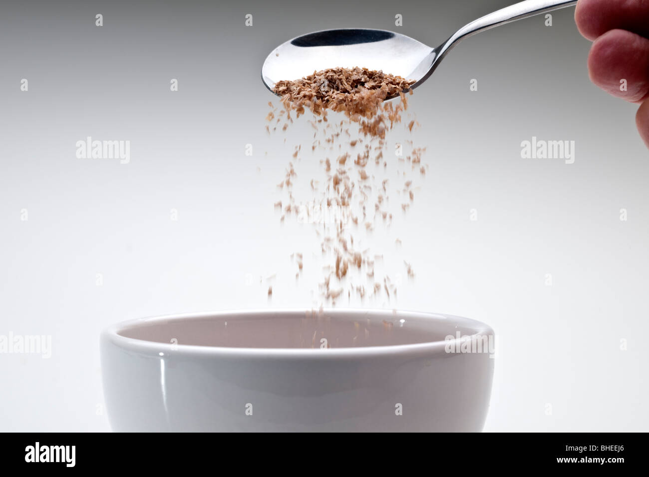 White cereal dish and wheat bran spilling from a heaped dessert spoon ...