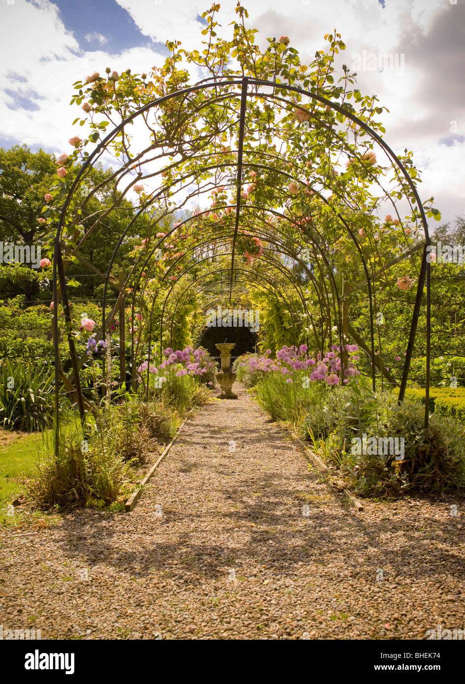 Metal rose arch over a gravel path with a sundial in the distance Stock ...