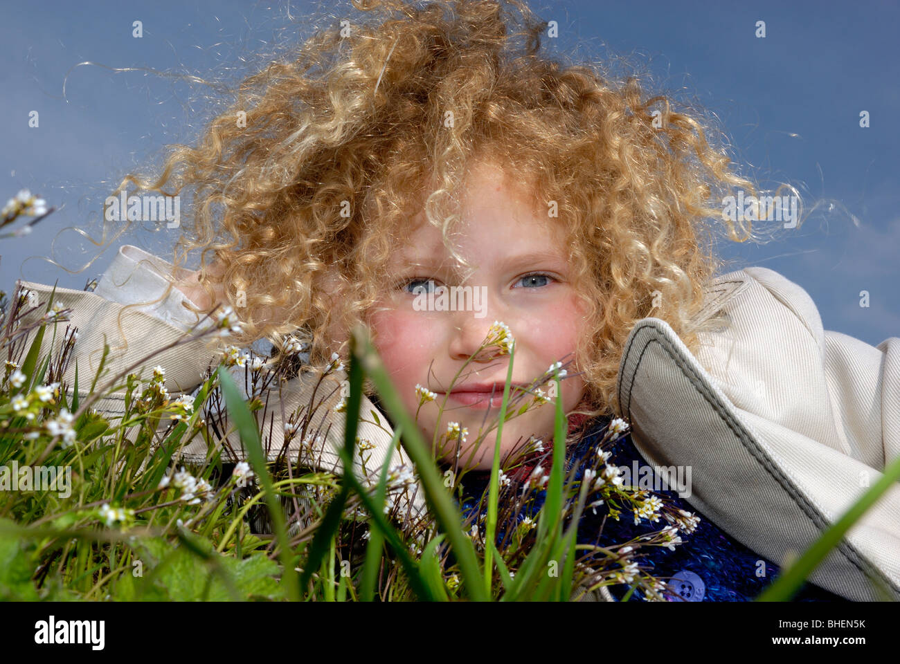 young girl with curly hair laying in grass with wild flowers in early ...