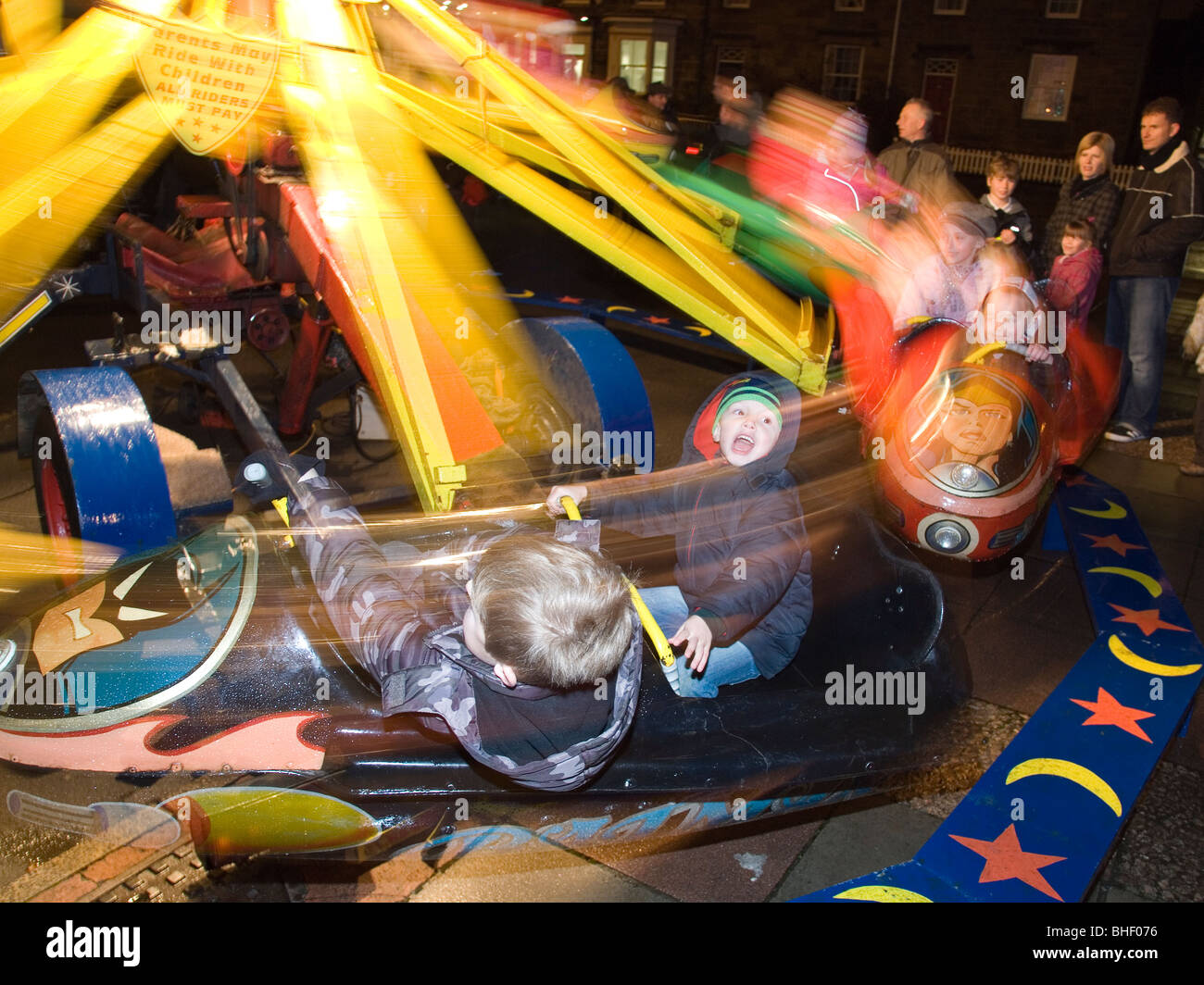 Parents watch excited children on a small fairground roundabout ...