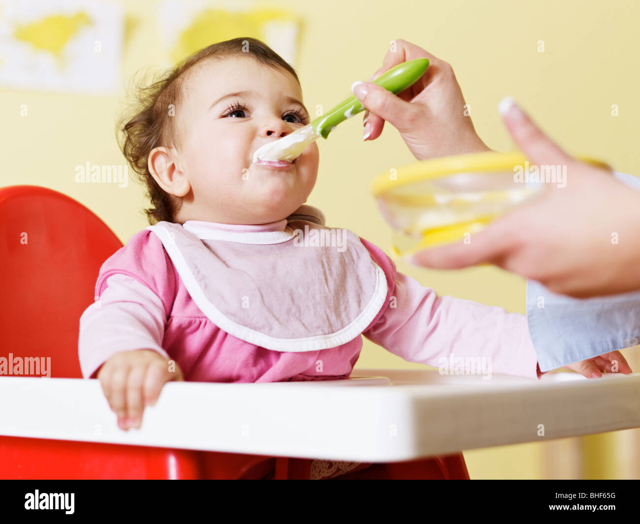 mom giving homogenized food to her daughter on high chair. Horizontal ...