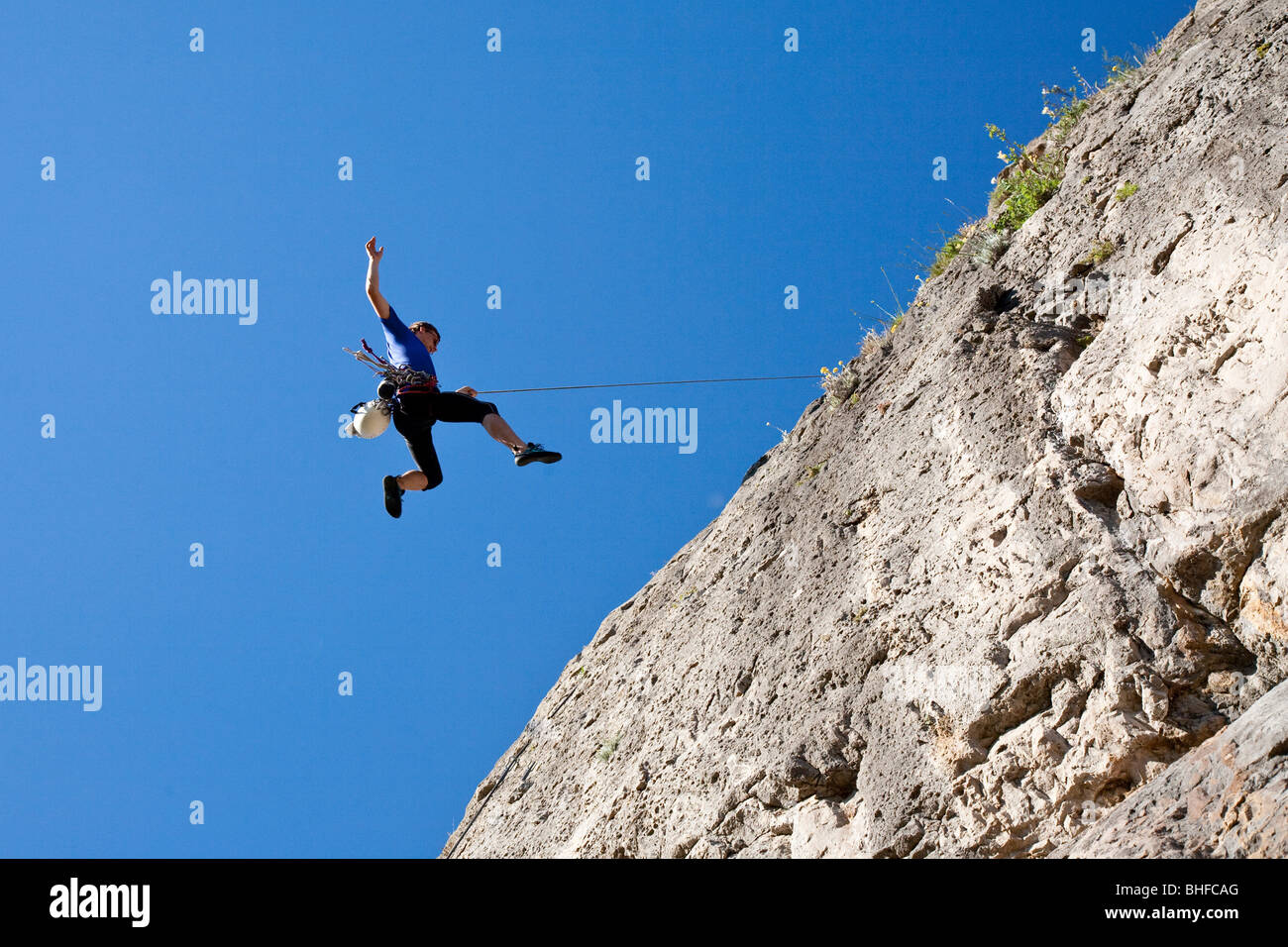 Rock climber abseiling from a rock face under blue sky, Jerzu, Sardinia ...