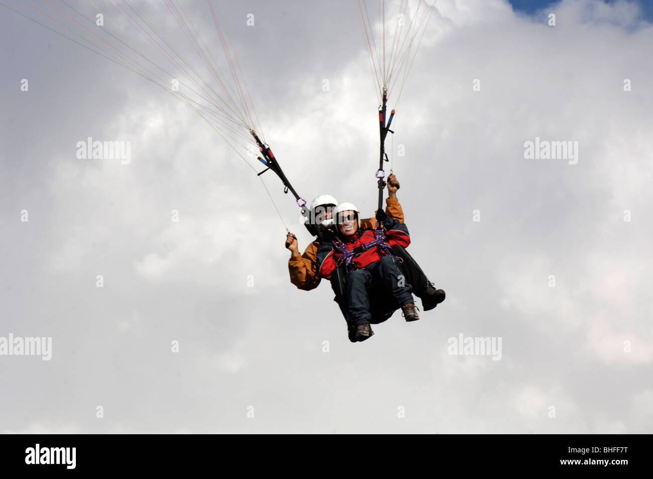 Two persons at tandem flight with paraglider in front of clouded sky ...