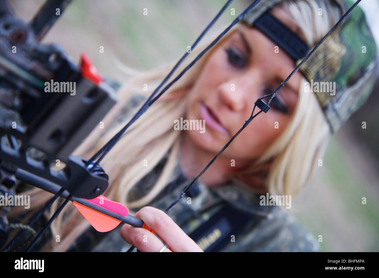 YOUNG WOMAN 21 Y.O. FEMALE HUNTER SITTING ON LOG PREPARING 80 POUND BOW ...