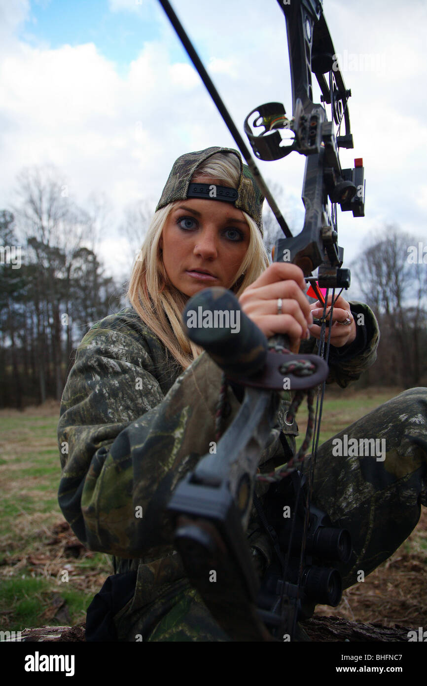 YOUNG WOMAN 21 Y.O. FEMALE HUNTER SITTING ON LOG PREPARING 80 POUND BOW ...