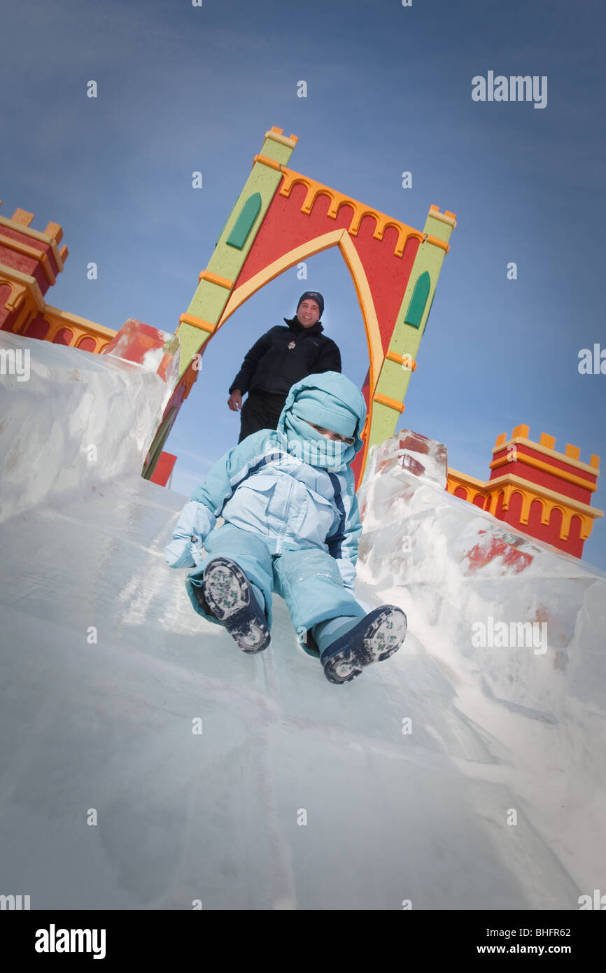 a kid rides an ice slide as her father looks on at the Quebec Winter ...