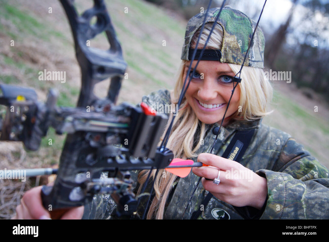 YOUNG WOMAN 21 Y.O. FEMALE HUNTER SITTING ON LOG PREPARING 80 POUND BOW ...