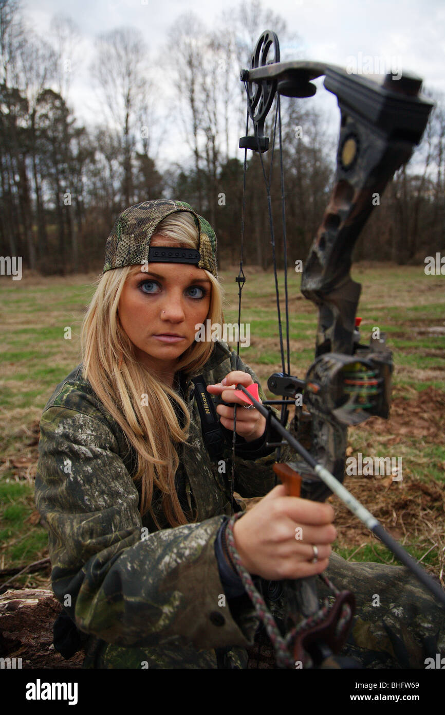 YOUNG WOMAN 21 Y.O. FEMALE HUNTER SITTING ON LOG PREPARING 80 POUND BOW ...
