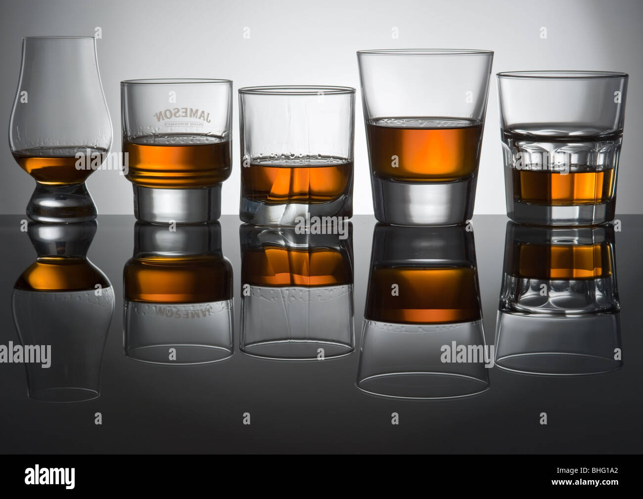 Five glasses with alcohol stand on glass. All glasses are reflected in ...