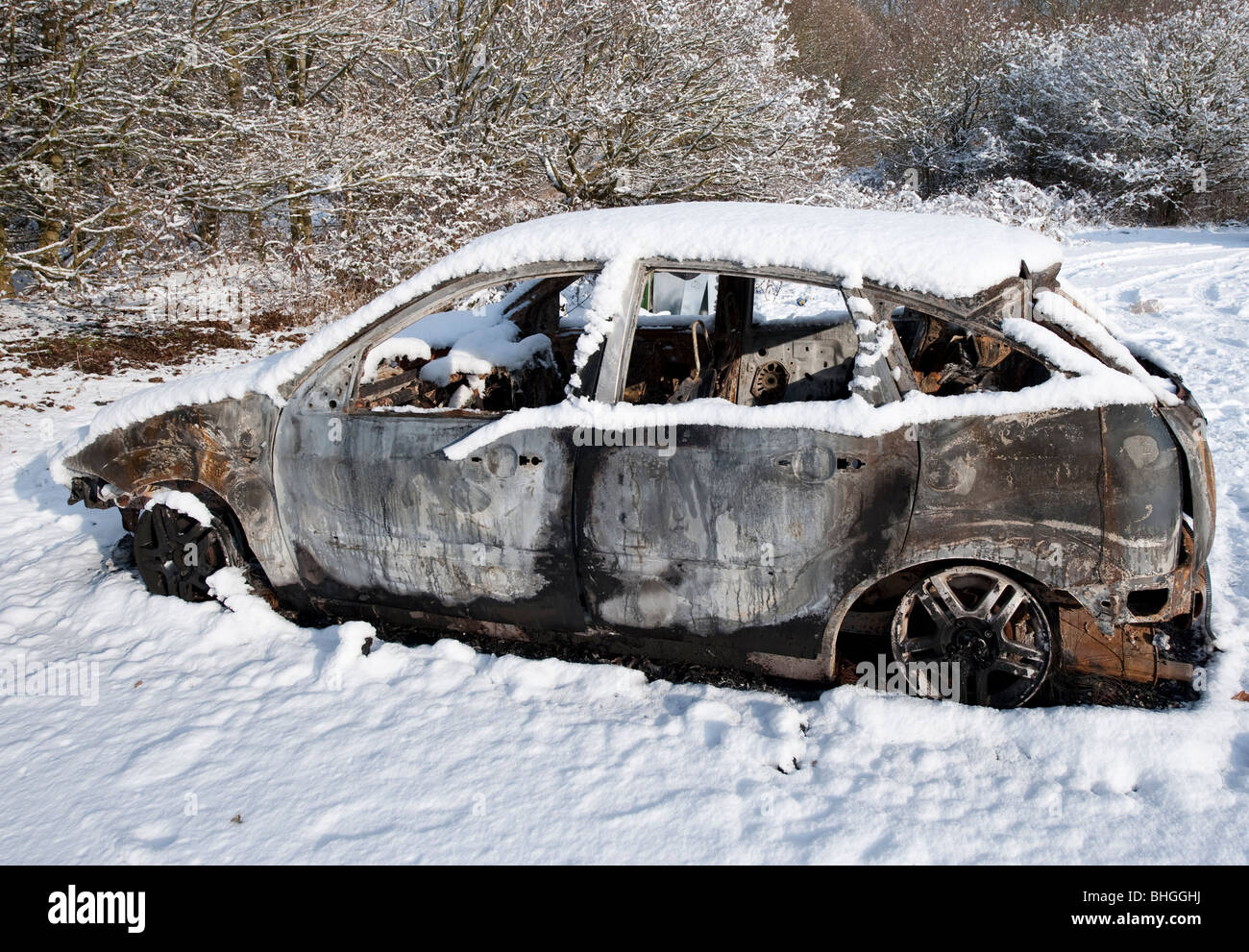 Abandoned burnt-out Ford motor car in car park and covered in snow ...