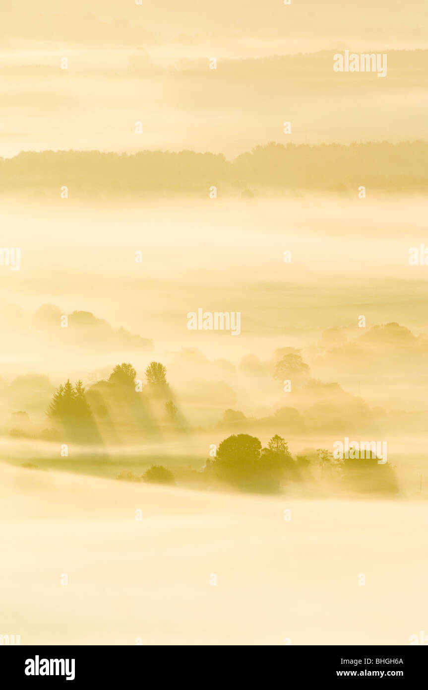 Inversion fog in the early morning lying over farmland and woods in the ...