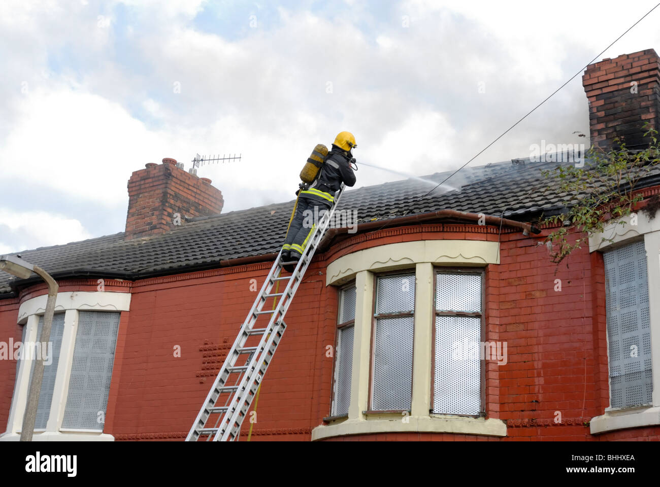 Fireman tackling fire in roof of terraced house Stock Photo - Alamy