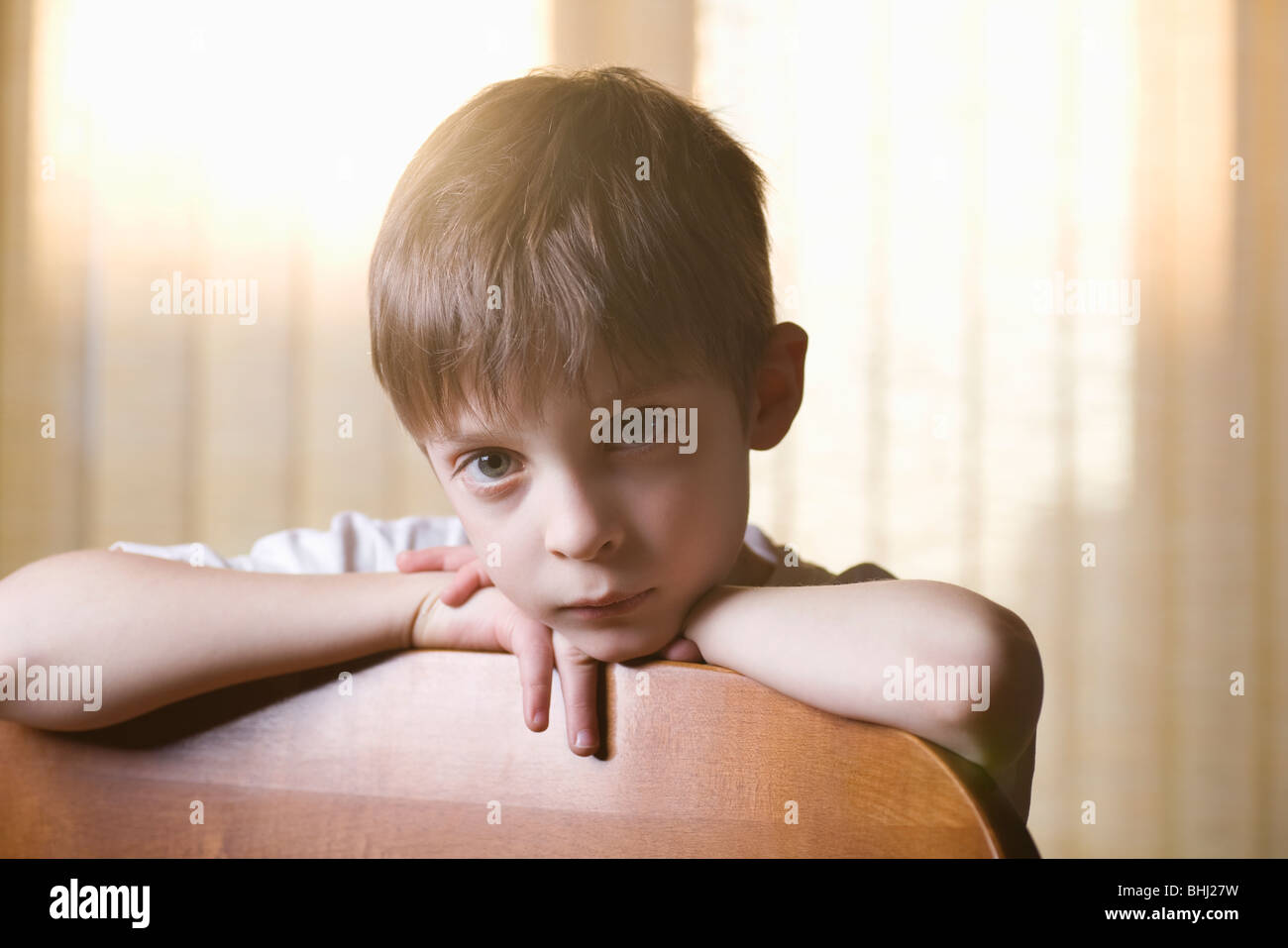 Boy sits looking at camera, leaning on chair back Stock Photo - Alamy