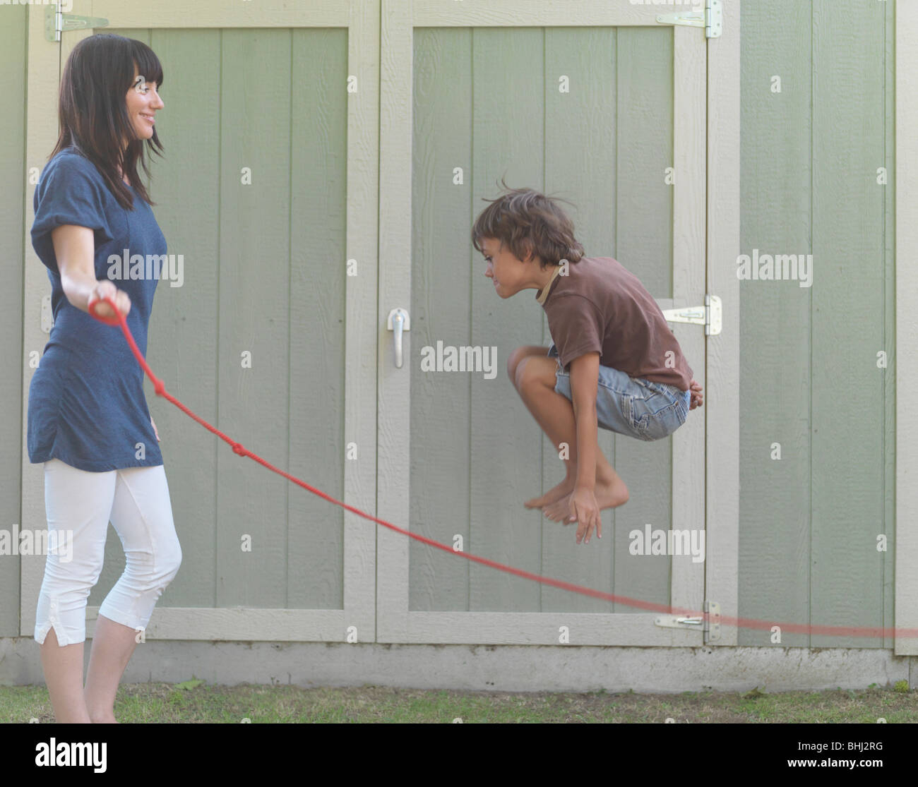Young boy jumping rope with mother Stock Photo - Alamy