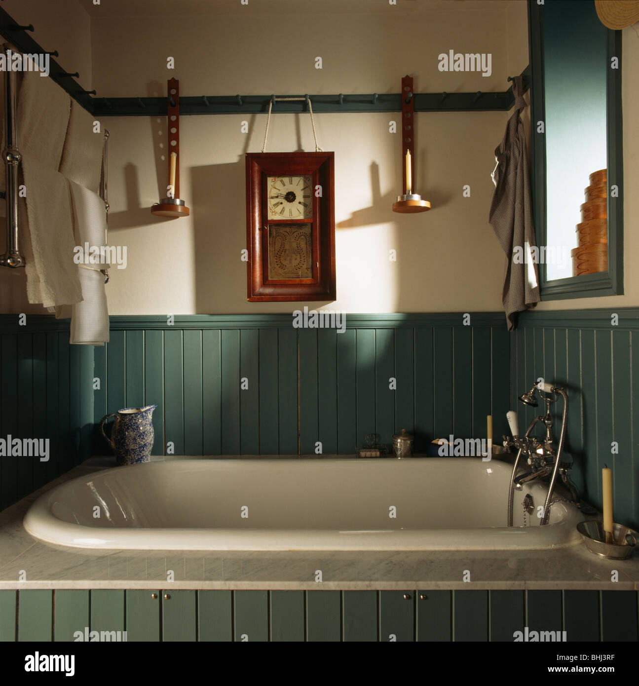 Wooden clock and candlesticks on peg-rail above bath in turquoise green ...