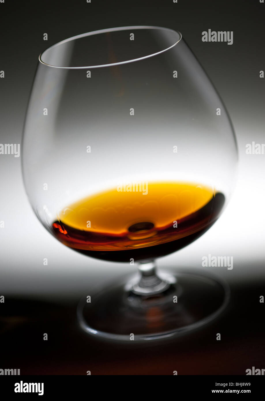 Glass with cognac against from white to the dark. Cognac drops flow ...