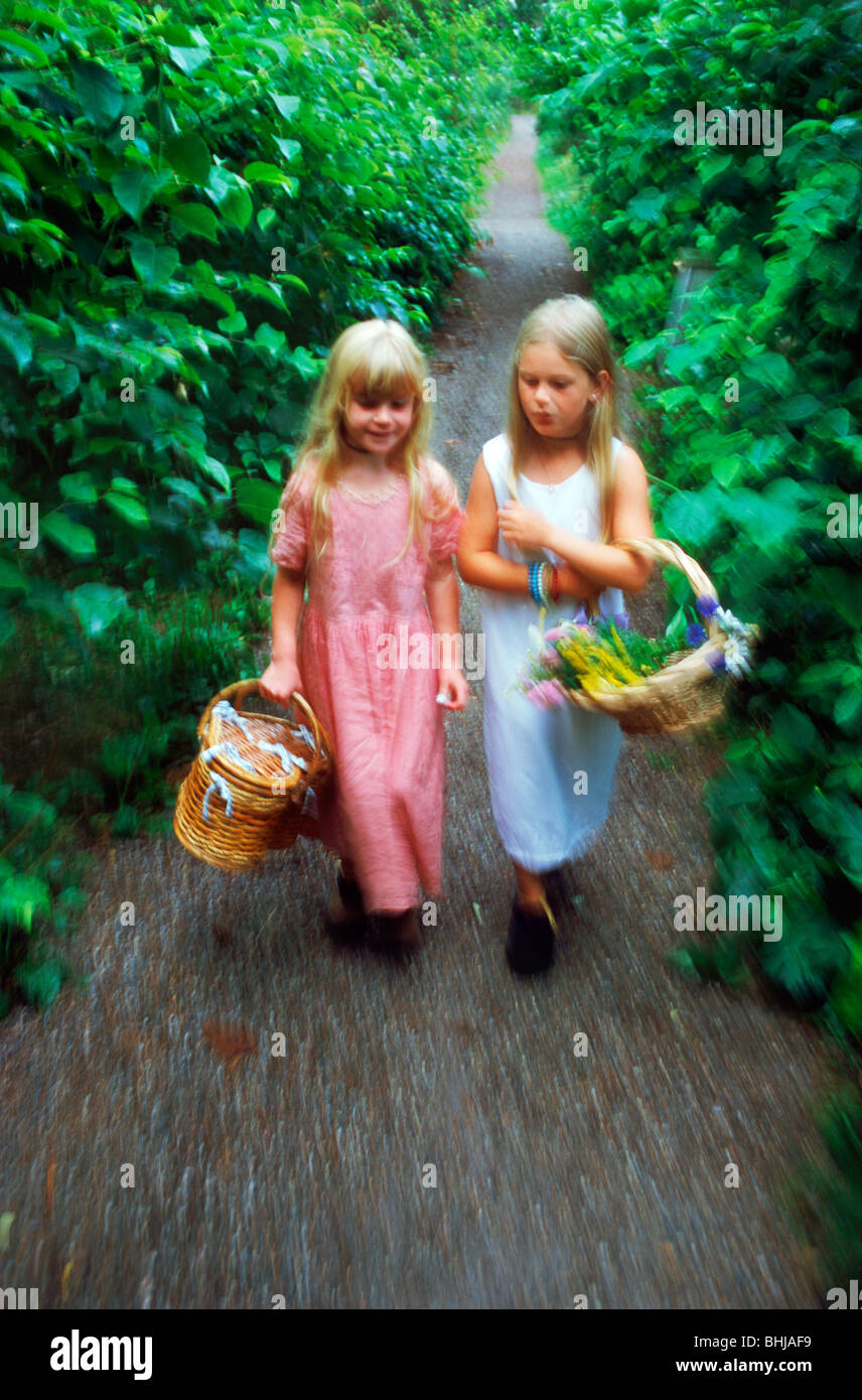 Two young girls on narrow pathway with summer dresses and baskets of ...