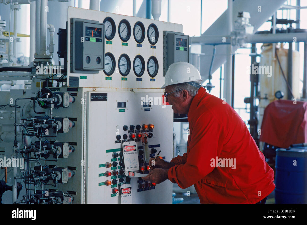Supervisor with hard hat checking control panel readings on offshore ...